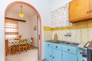Uma cozinha com armário azul, mesa de madeira com cadeiras e luminária pendente.