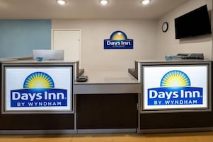 Uma receção com dois ecrãs a exibir o logótipo da Days Inn, um relógio e uma televisão de ecrã plano na parede.