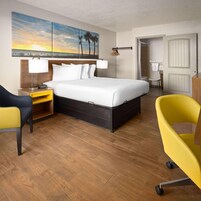 Quarto de hotel com cama, mesas de cabeceira, escrivaninha, cadeira e um quadro na parede.