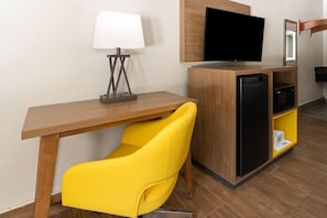 Quarto de hotel com escrivaninha de madeira, uma cadeira amarela, televisão de tela plana, frigorífico e micro-ondas.