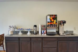 Uma bancada de cozinha com máquina de café, dispensador de suco e diversos alimentos.