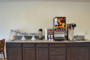 Uma bancada de cozinha com máquina de café, dispensador de suco e diversos alimentos.