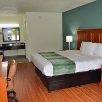 Quarto de hotel com cama, escrivaninha, cadeira, luminária e espelho.