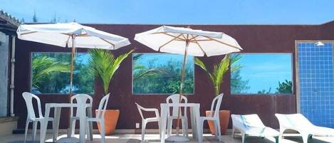 Área de piscina com espreguiçadeiras e guarda-sóis, cercada por um revestimento de azulejos e vista para o verde.