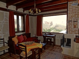 Quarto aconchegante com parede de pedra, teto de madeira, sofá, mesa de jantar e lareira.