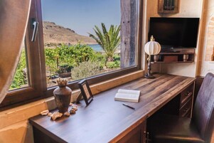 Uma mesa de madeira com vista para uma praia e colinas, uma televisão e um abajur.