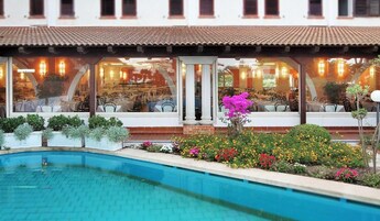 Área de piscina com espaço coberto para relaxar, rodeada por vasos de plantas e flores.