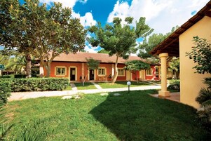 Uma casa com telhado vermelho, um jardim com gramado e uma árvore, e um caminho que leva à entrada.