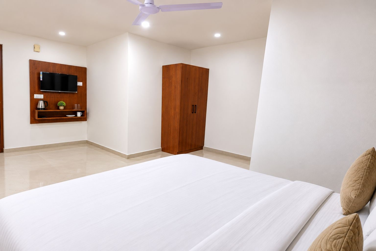 Quarto com cama, guarda-roupa, televisão fixada na parede e ventoinha de teto.