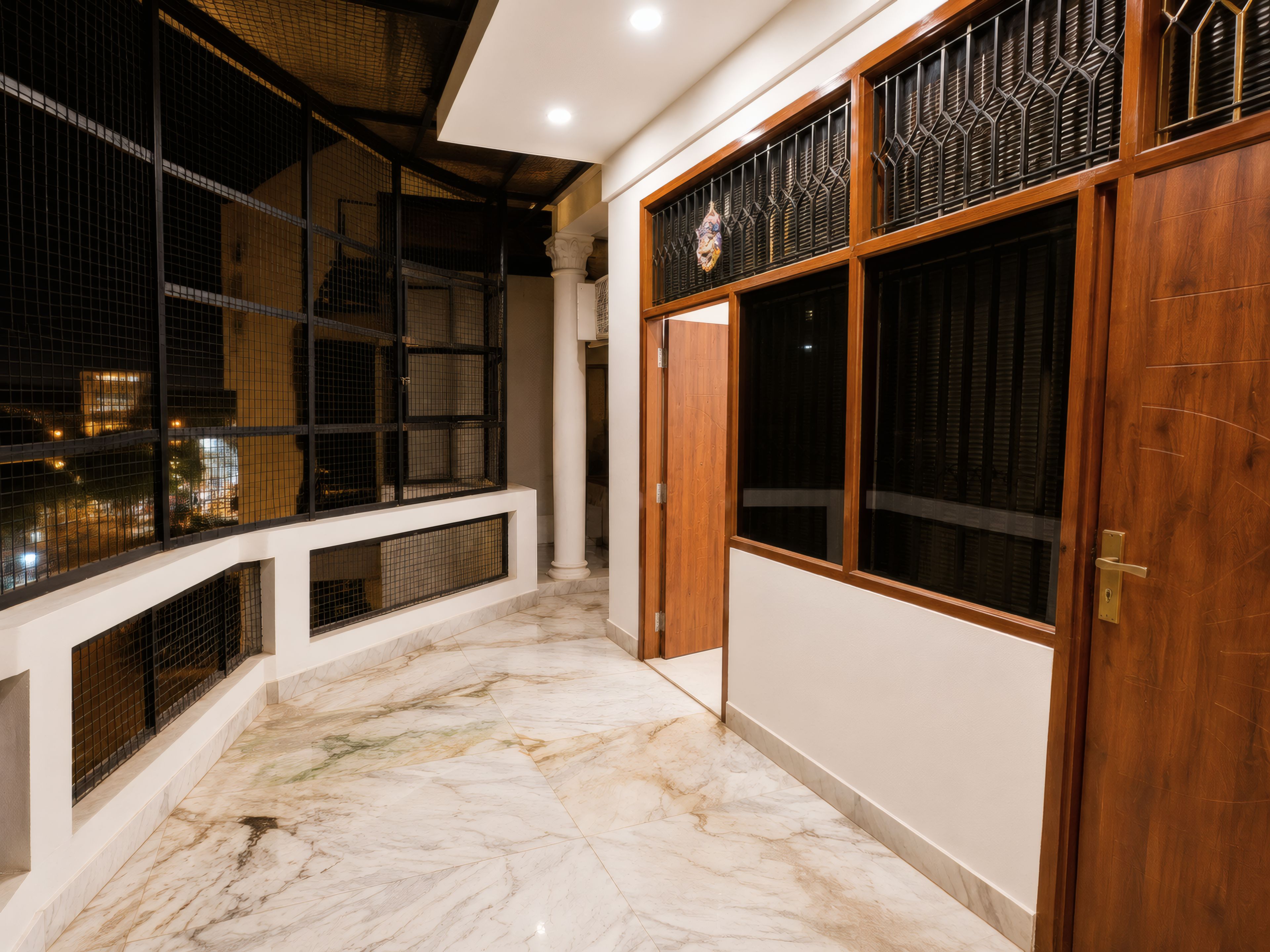 Um corredor com piso de mármore, porta de madeira e janela com grade decorativa.