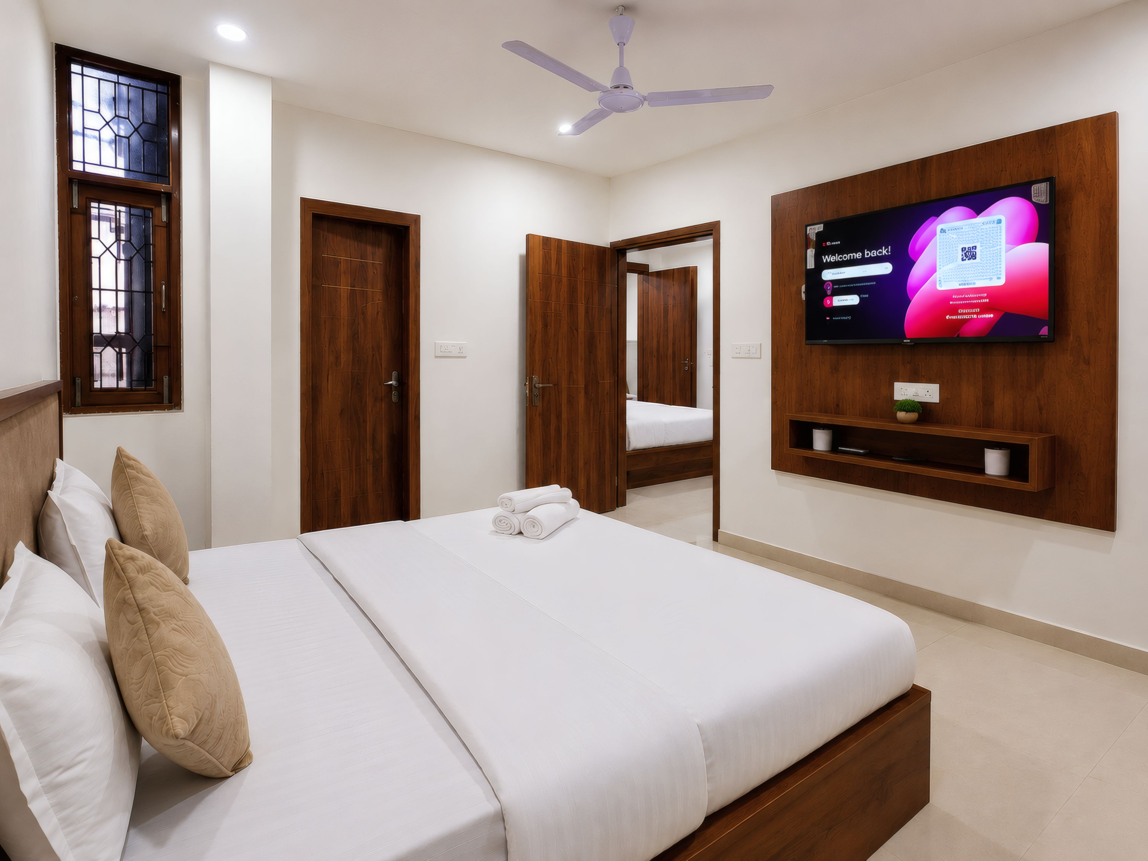 Quarto de hotel com uma cama, televisão na parede e ventilador de teto.