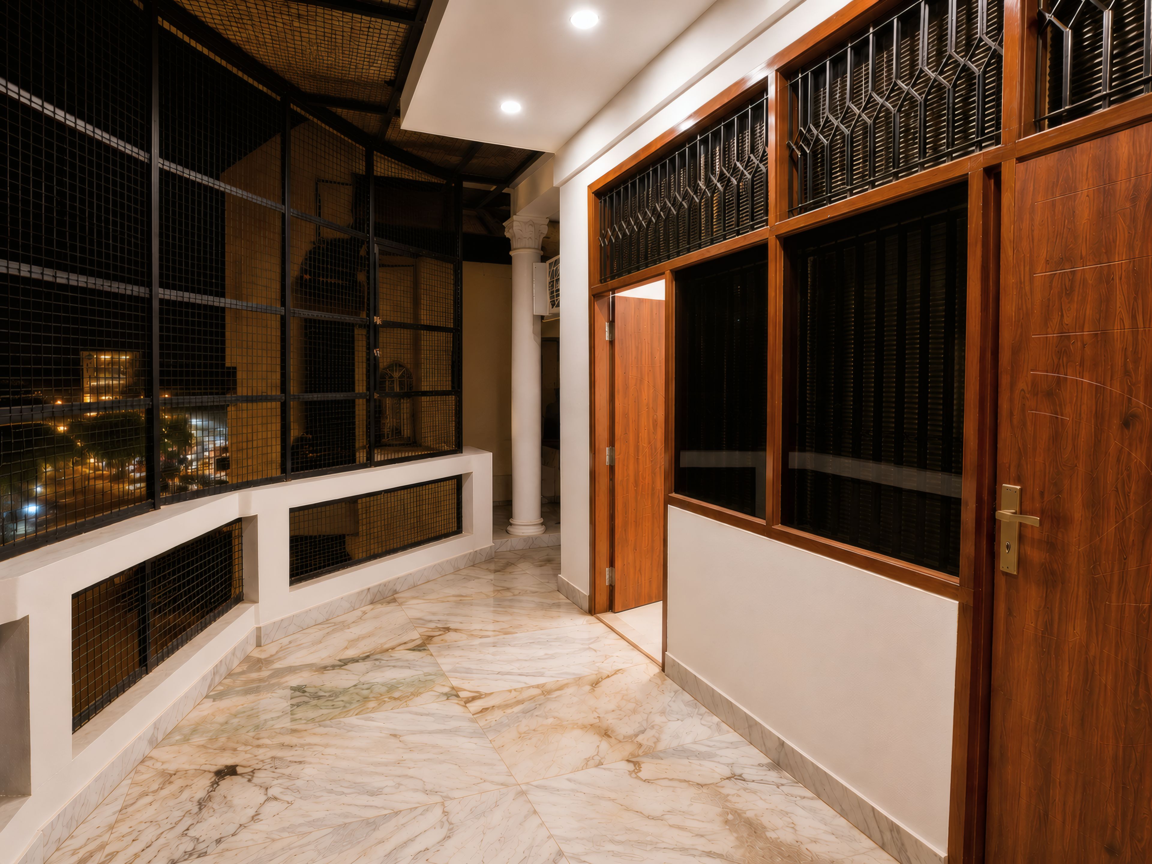 Um corredor com piso de mármore, porta de madeira e janela com grade de metal.