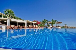 Piscina com espreguiçadeiras e guarda-sóis, cercada por palmeiras e um céu ensolarado.