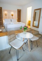 Quarto de hotel com cama, duas cadeiras, uma mesa e um espelho.