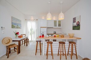 Cozinha moderna com armários brancos, ilha central com banquetas, luminárias pendentes e obras de arte nas paredes.