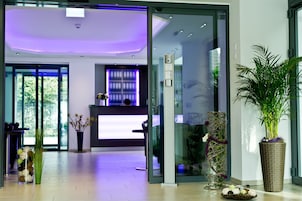 Uma área de recepção moderna com entrada por porta de vidro, balcão de atendimento e uma grande planta em vaso.
