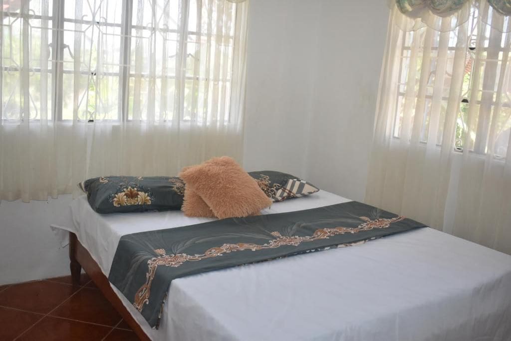 Quarto com cama, cortinas e vista pela janela.
