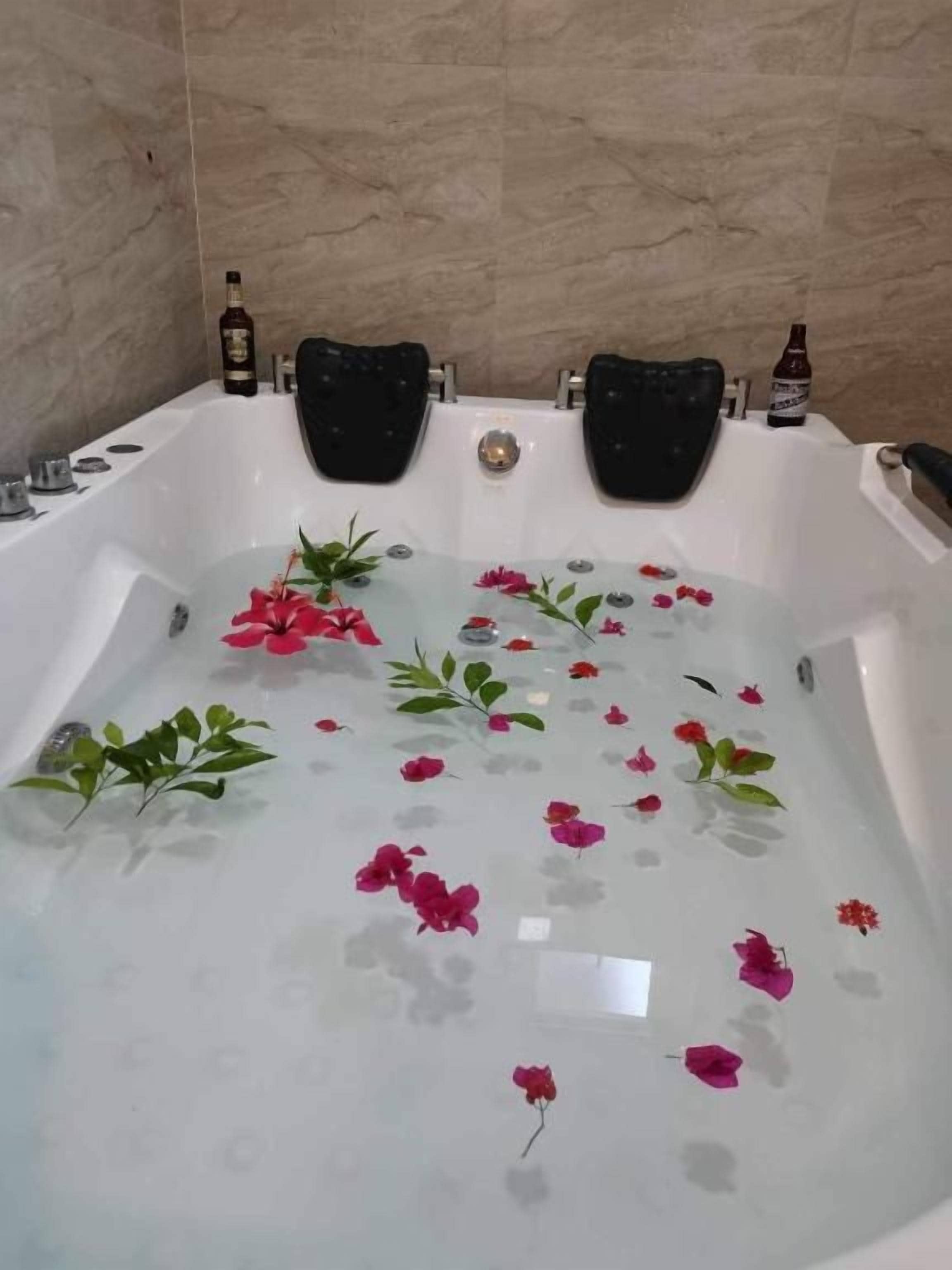 Uma banheira com água, flores boiando e duas garrafas de álcool.