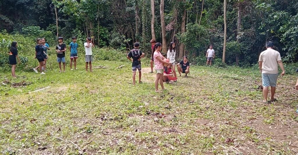 Um grupo de pessoas em ambiente externo, com árvores e grama.