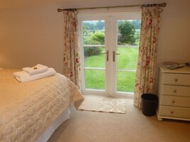 Quarto com cama, penteadeira, janela com cortinas e vista para um jardim.