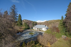 Uma casa com uma entrada ampla, cercada por árvores e uma montanha ao fundo.