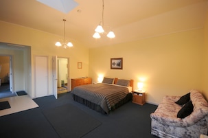 Um quarto com cama, mesas de cabeceira, uma cadeira e um quadro na parede.