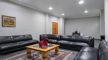 Uma sala de estar com dois sofás de couro preto, uma mesa de centro de madeira e um tapete estampado.