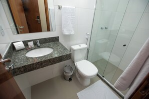 Casa de banho moderna com lavatório em granito, sanita e cabine de duche com parede de vidro.