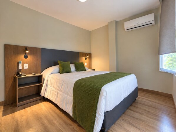 Quarto de hotel com cama, mesas de cabeceira, ar condicionado na parede e uma janela.