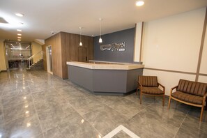 Uma área de recepção de hotel com balcão, duas cadeiras e uma escadaria ao fundo.