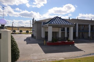 Hotel com entrada coberta, estacionamento e céu limpo.