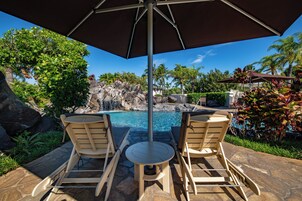 Área da piscina com duas espreguiçadeiras, uma mesa e um guarda-sol.