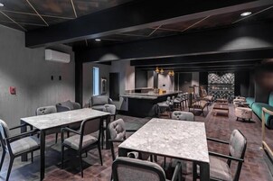 Um restaurante moderno com mesas e cadeiras de mármore, área de bar e um espaço de estar com sofás e pufes.