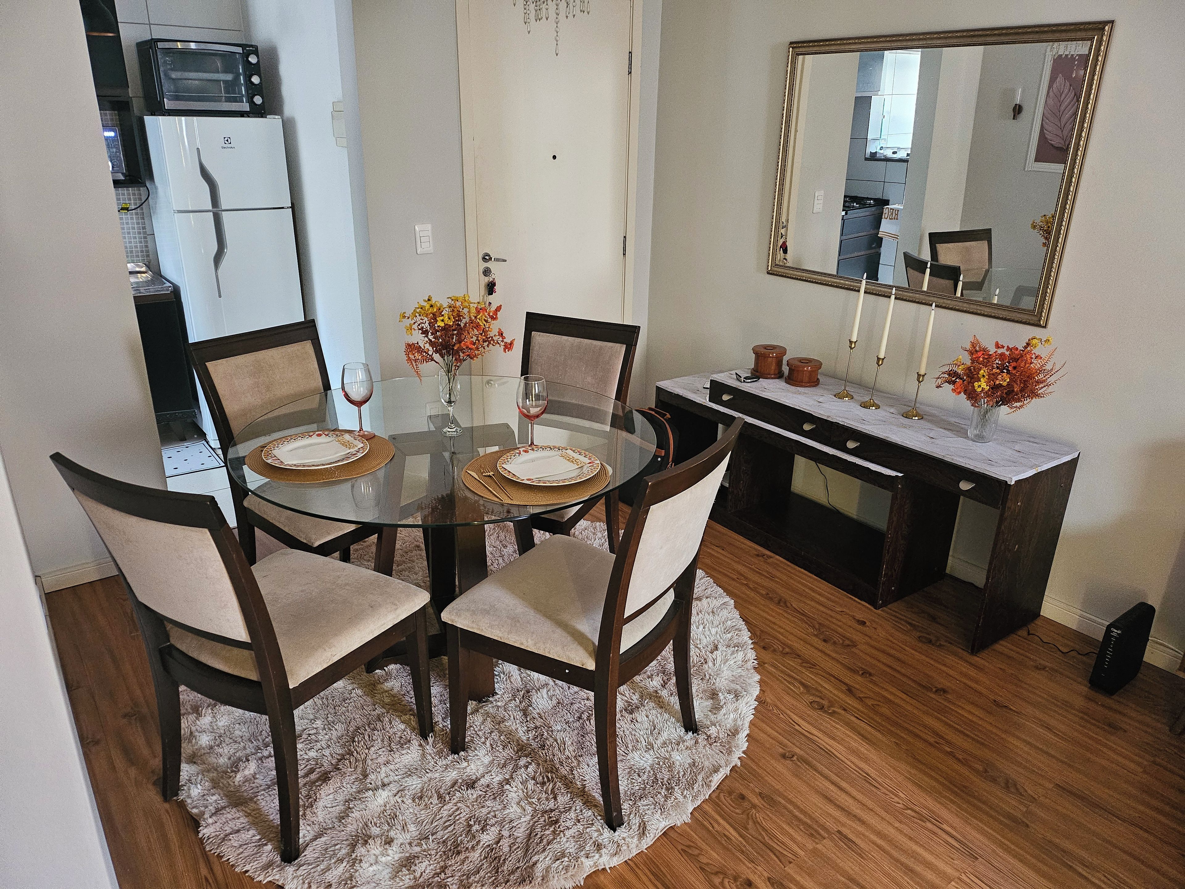 Uma área de refeições com mesa de vidro, quatro cadeiras e um vaso decorativo com flores.