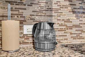 Uma cozinha com chaleira de aço inoxidável sobre bancada de granito, rolo de papel toalha e backsplash de mosaico.