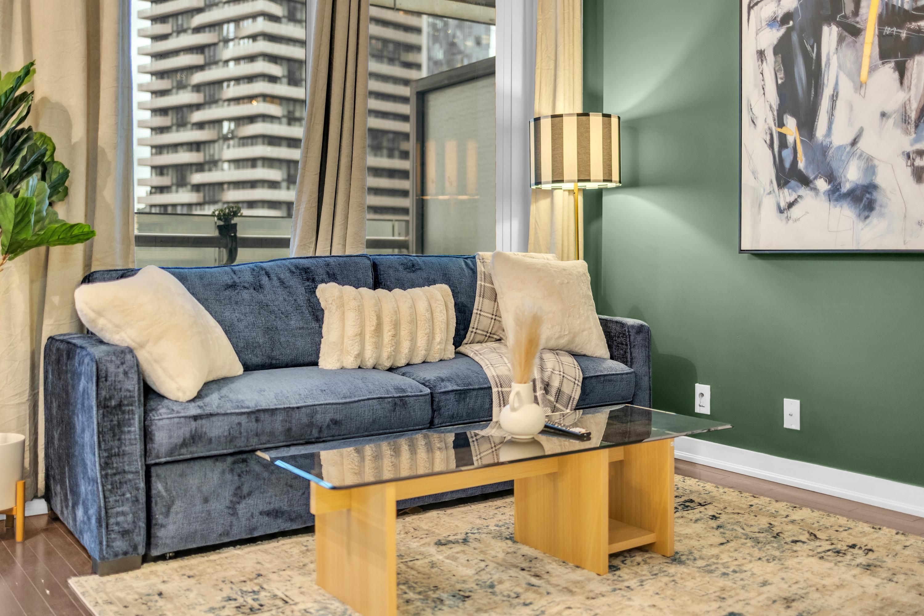 Uma sala de estar moderna com um sofá azul, uma mesa de centro de vidro e uma parede verde.