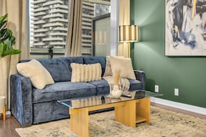 Uma sala de estar moderna com um sofá azul, uma mesa de centro de vidro e uma parede verde.