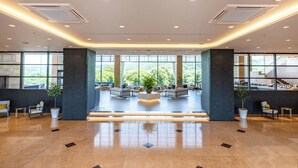 Um hall amplo com área de estar central, janelas grandes com vista para o verde e piso de azulejo polido.