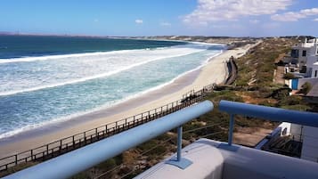 Vista costeira com praia, grades e edifícios ao fundo.