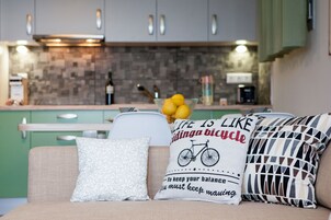 Sala de estar com sofá, três almofadas decorativas e cozinha ao fundo.