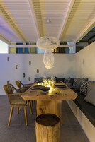 Uma área de refeições ao ar livre com uma mesa de madeira, cadeiras e um lustre suspenso.