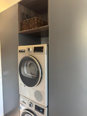 Máquina de lavar e secar compacta, fixada na parede, com painel de controle e cesto superior.