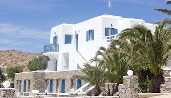 Edifício branco com venezianas azuis, paredes de pedra e varanda.