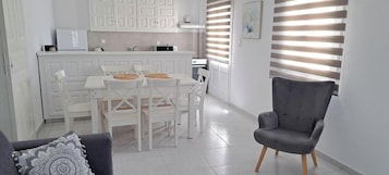 Cozinha moderna com armários brancos, uma mesa de jantar com cadeiras e uma poltrona cinza.