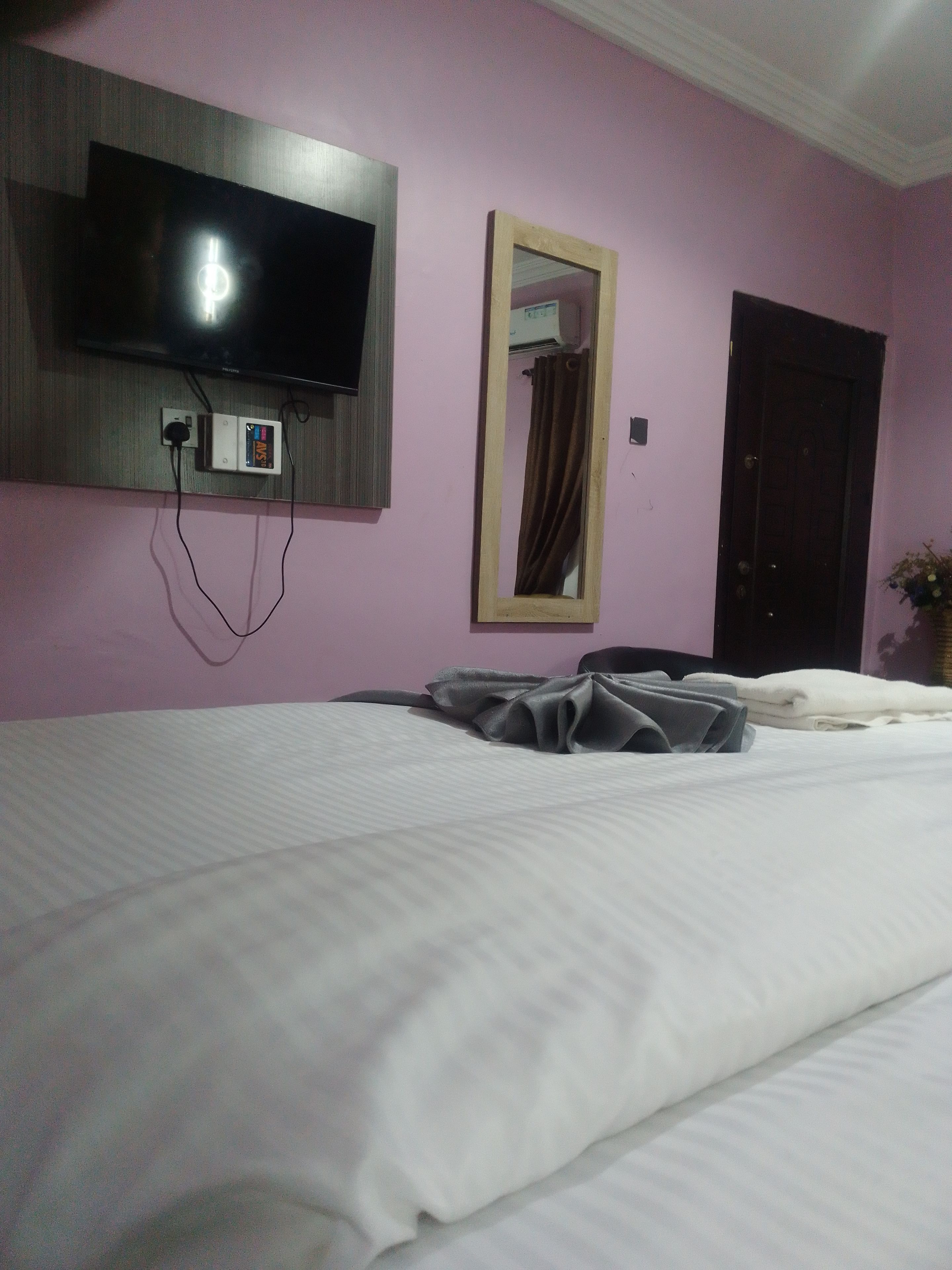 Quarto de hotel com cama, televisão de tela plana na parede, espelho e porta.