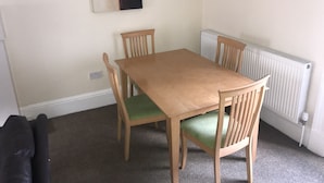Uma pequena sala de jantar com mesa de madeira e quatro cadeiras, um radiador e uma tomada na parede.