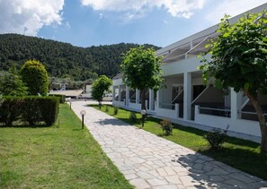 Um caminho conduz a um edifício com arquitetura moderna, cercado por vegetação e com montanhas ao fundo.