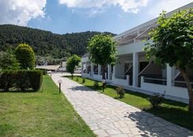 Um caminho conduz a um edifício com arquitetura moderna, cercado por vegetação e com montanhas ao fundo.