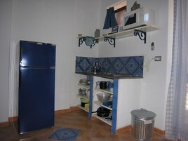 Cozinha compacta com geladeira azul, micro-ondas em uma prateleira e lixeira.