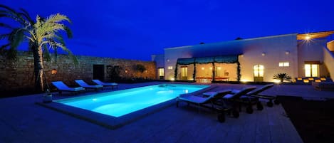 Piscina com espreguiçadeiras e uma parede de pedra.